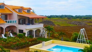 Uma casa grande de dois andares com piscina, rodeada por vegetação e céu claro.