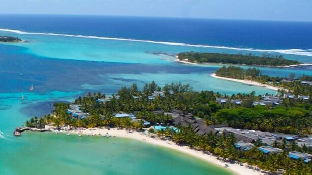 Uma área costeira com praia, águas cristalinas e um pequeno povoado com edifícios.