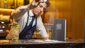 Um bartender preparando uma bebida com um coqueteleira e um copo de cocktail sobre um balcão de mármore.