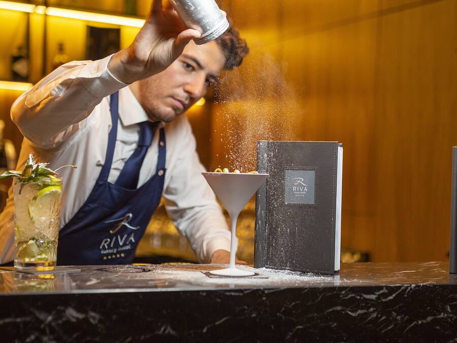 Um bartender preparando uma bebida com um coqueteleira e um copo de cocktail sobre um balcão de mármore.