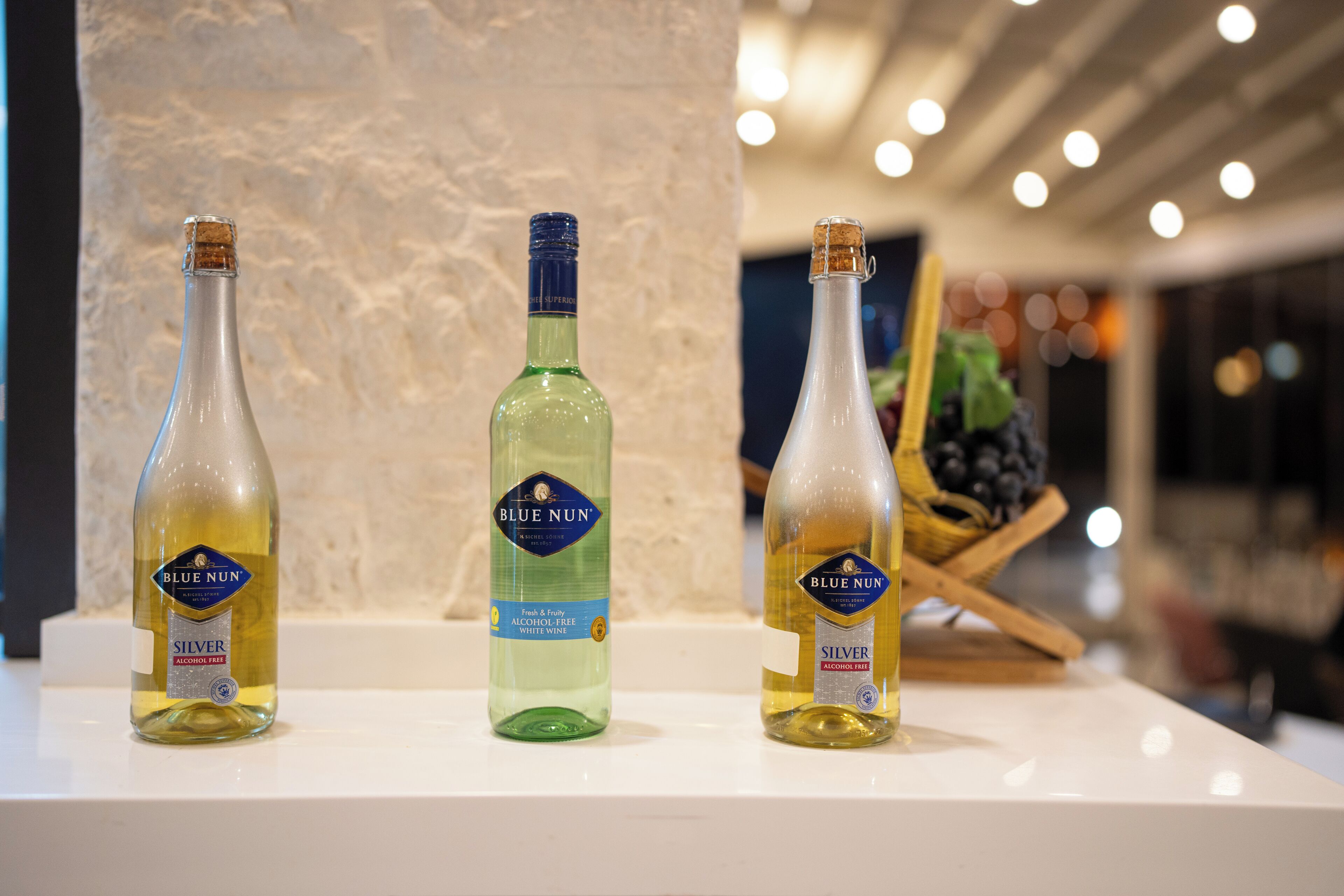 Três garrafas de vinho Blue Nun Silver sobre uma superfície branca.