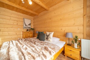 Quarto de cabana de madeira com cama, mesa de cabeceira, abajur e um quadro na parede.