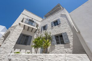 Um edifício branco com varanda e persianas, rodeado por vegetação.