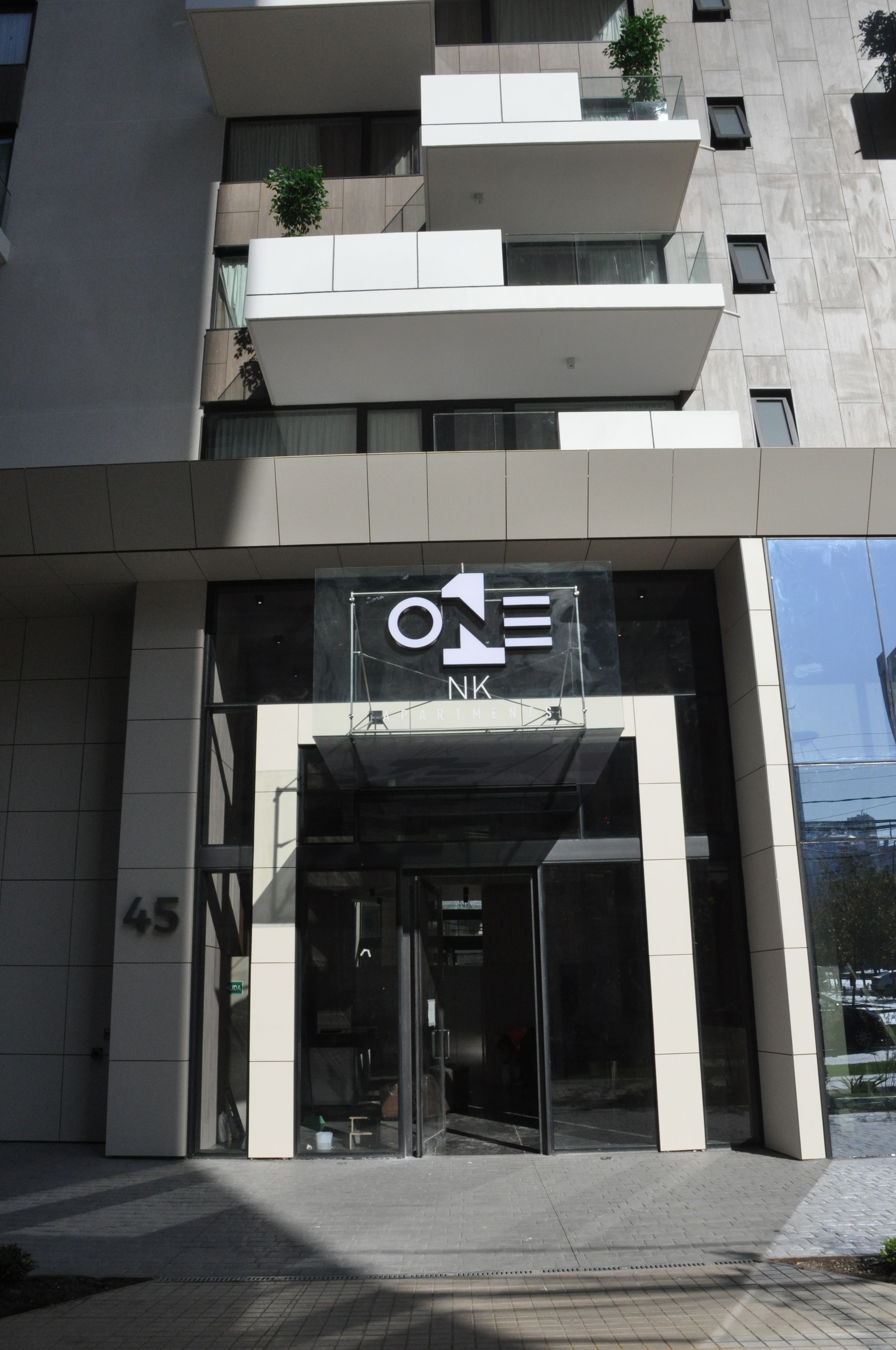 Um edifício moderno com entrada de vidro, uma placa com a inscrição "ONE NK" e o número "45" na lateral.