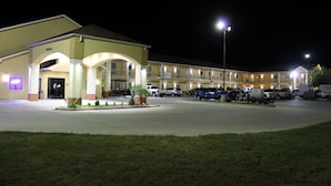Um motel com pátio central, vários espaços de estacionamento e entrada bem iluminada.