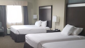 Quarto de hotel com duas camas, uma escrivaninha com abajur e um telefone.