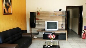 Uma sala de estar com um sofá, uma televisão, uma mesa de centro com flores e uma lareira.