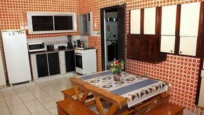 Cozinha compacta com eletrodomésticos brancos, mesa de madeira com bancos e papel de parede estampado.