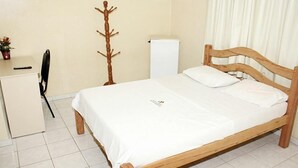Uma cama de solteiro com estrutura de madeira e roupa de cama branca em um quarto com piso de azulejos.