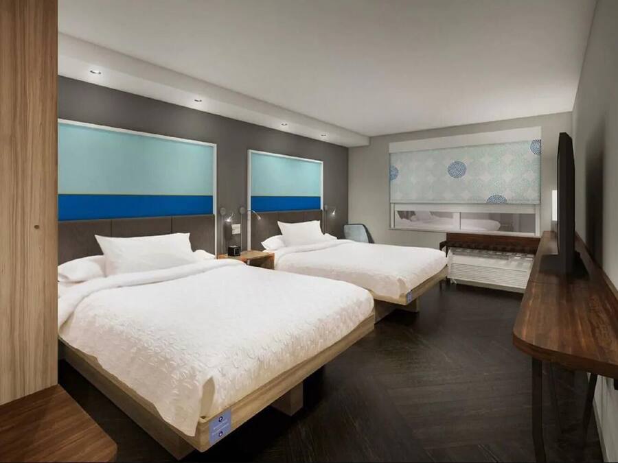 Quarto de hotel com duas camas, um espelho grande, televisão e banheiro com pia e espelho.