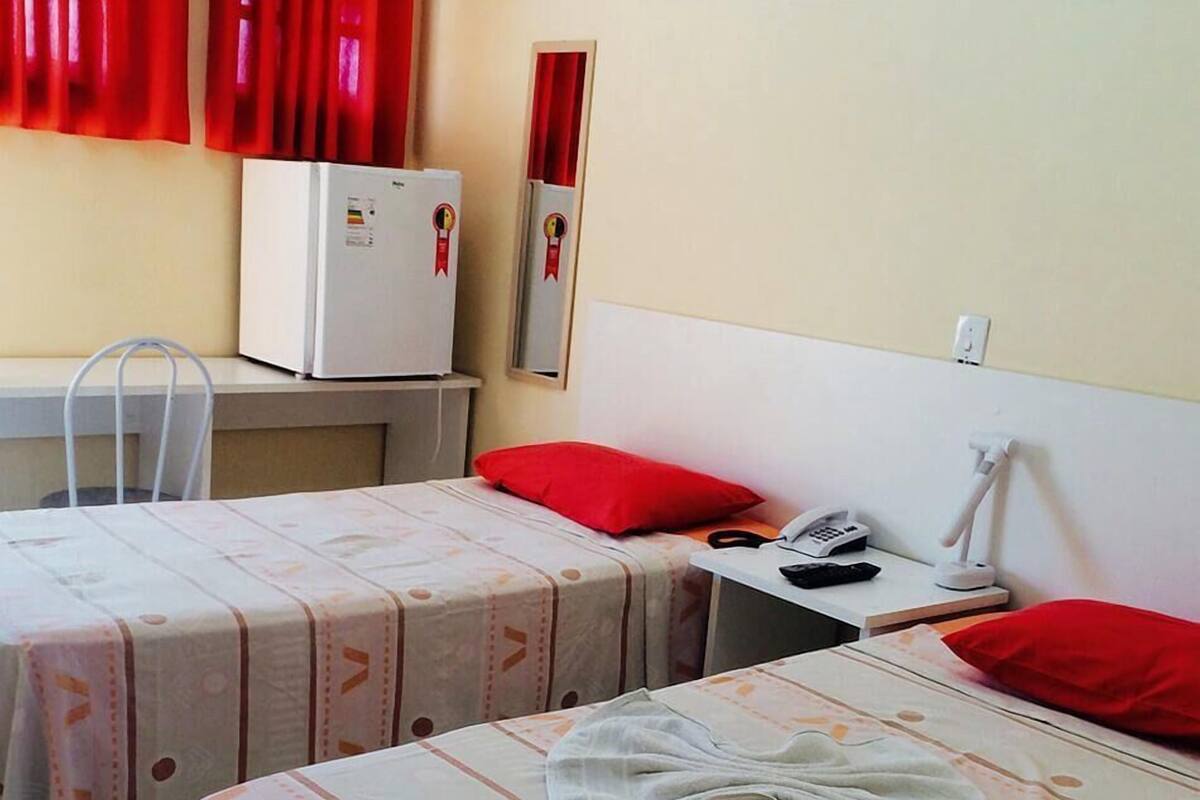 Quarto com duas camas, uma escrivaninha, uma cadeira, um telefone e uma luminária.