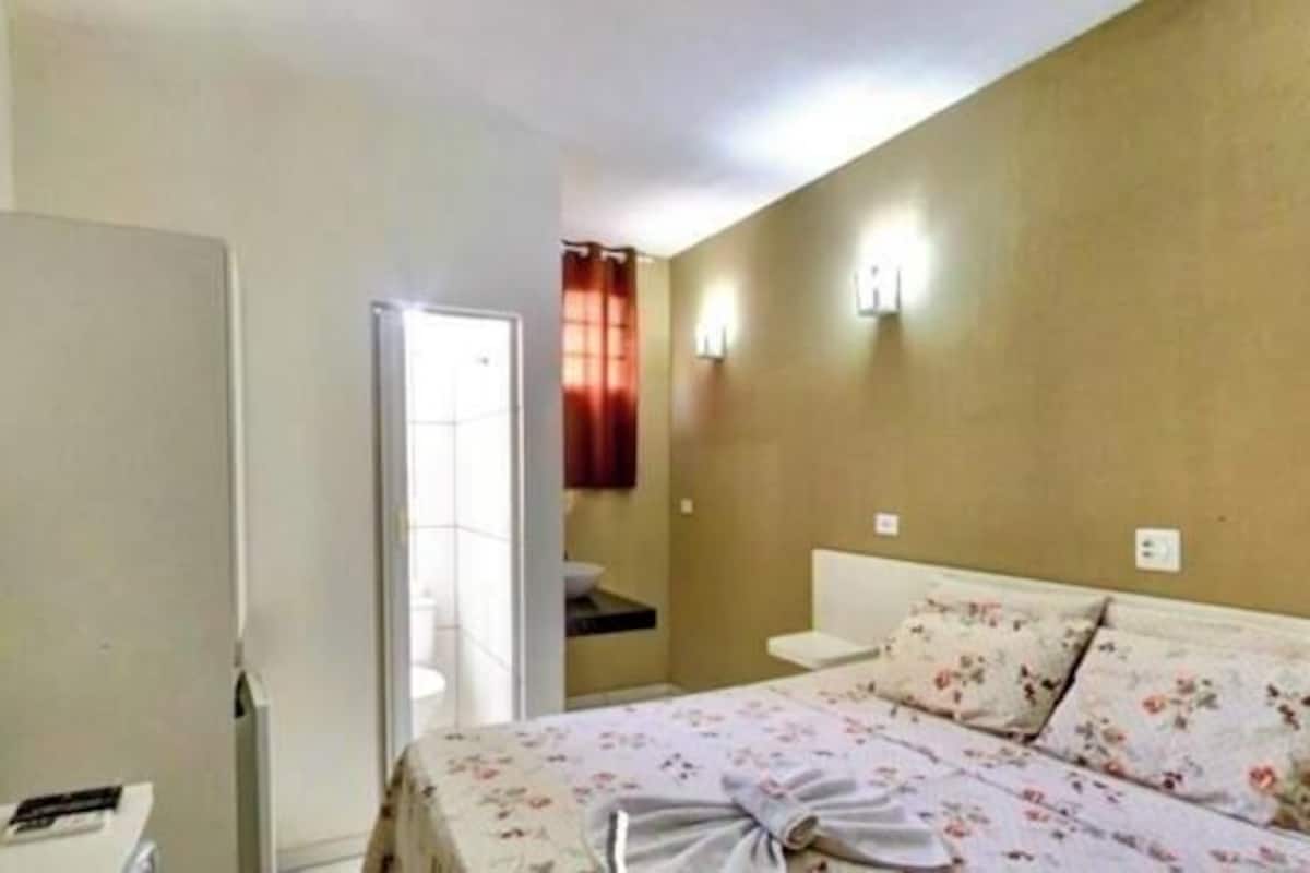 Quarto de hotel com cama, televisão, guarda-roupa e banheiro.