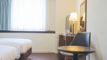 Quarto de hotel com uma cama, uma escrivaninha com abajur e uma cadeira.
