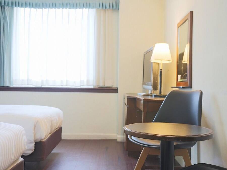 Quarto de hotel com uma cama, uma escrivaninha com abajur e uma cadeira.