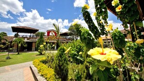 Um hotel com fachada vermelha e branca, área externa coberta e vegetação exuberante.