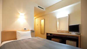 Quarto de hotel com uma cama, uma escrivaninha com televisão, um espelho e um pequeno armário.