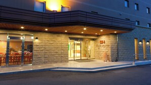 Entrada de hotel com fachada de pedra, portas de vidro e uma placa com a inscrição "EVER HOTEL".