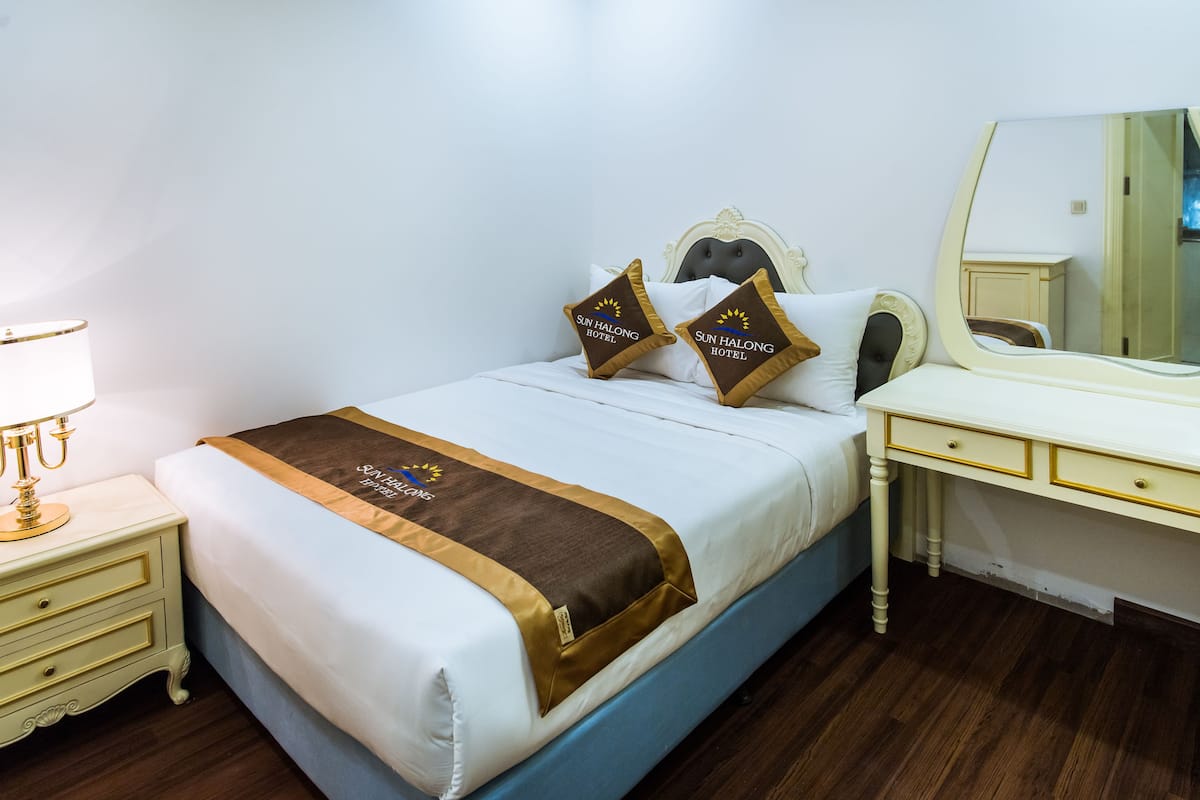 Quarto de hotel com uma cama, mesa de cabeceira, escrivaninha e espelho.