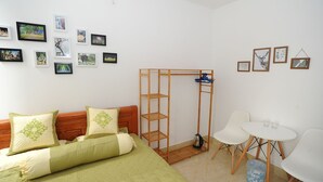 Quarto com cama, estante de madeira, mesa branca e cadeiras.