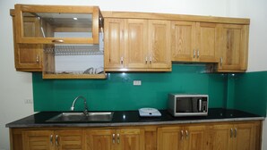 Cozinha com armários de madeira, bancada preta, pia de aço inoxidável e micro-ondas.