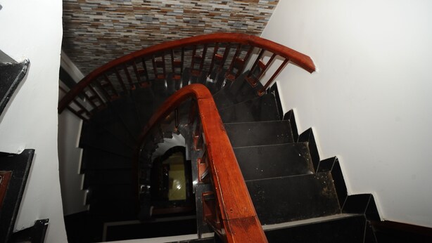 Uma escadaria em espiral com corrimão vermelho e degraus pretos, que dá acesso a um espaço com teto azulejado.