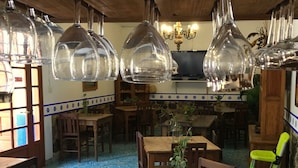 Uma sala de jantar com várias mesas e cadeiras, um lustre e copos pendurados.