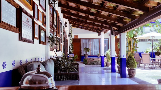 Um hall de hotel com teto de madeira, certificados emoldurados na parede, um balcão de recepção e plantas em vasos.