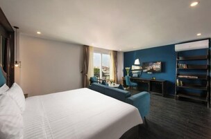 Quarto de hotel com uma cama grande, área de estar com escrivaninha e uma estante de livros.
