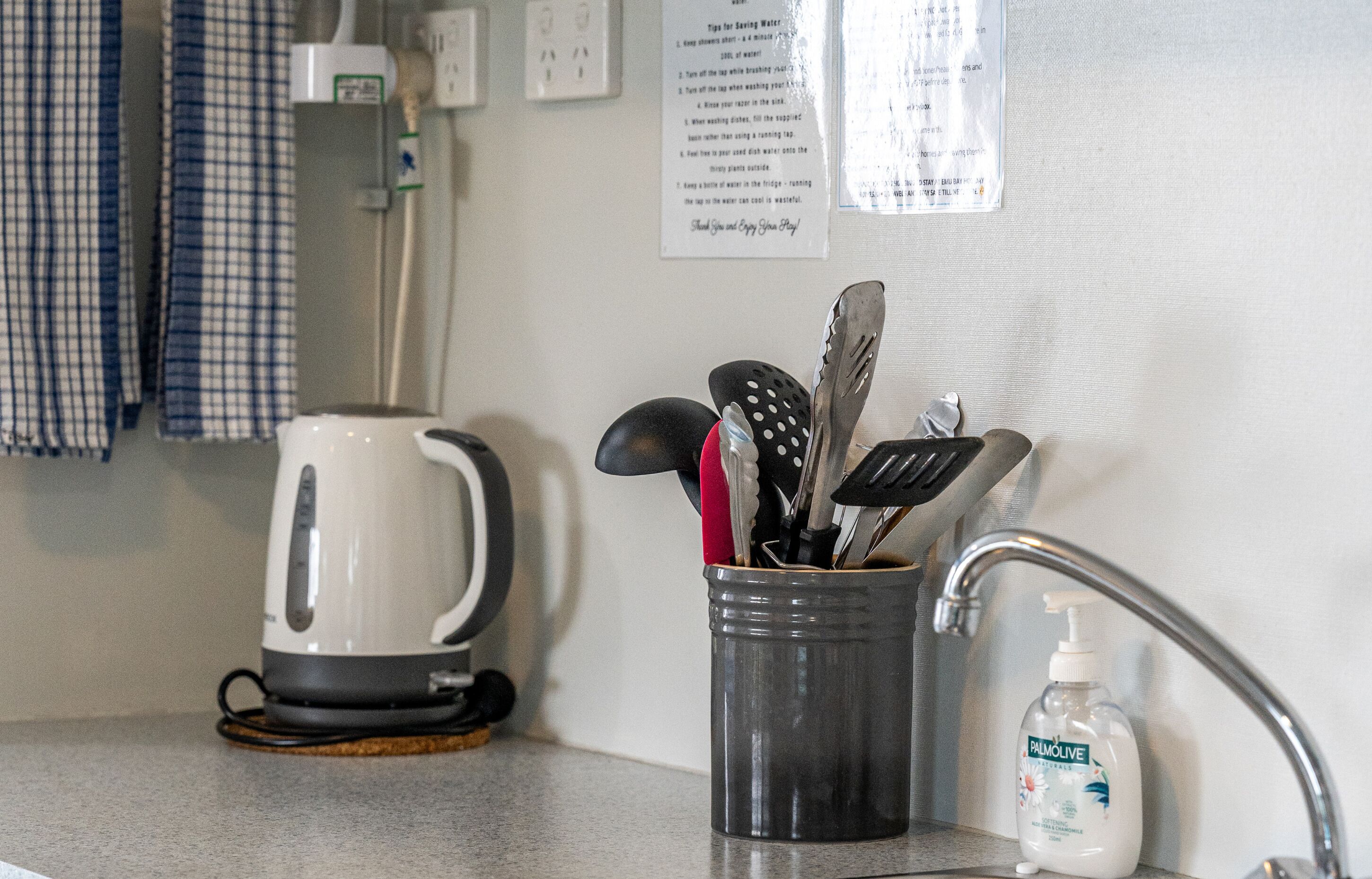 Uma bancada de cozinha com uma chaleira, um porta-utensílios e uma garrafa de sabonete Palmolive.