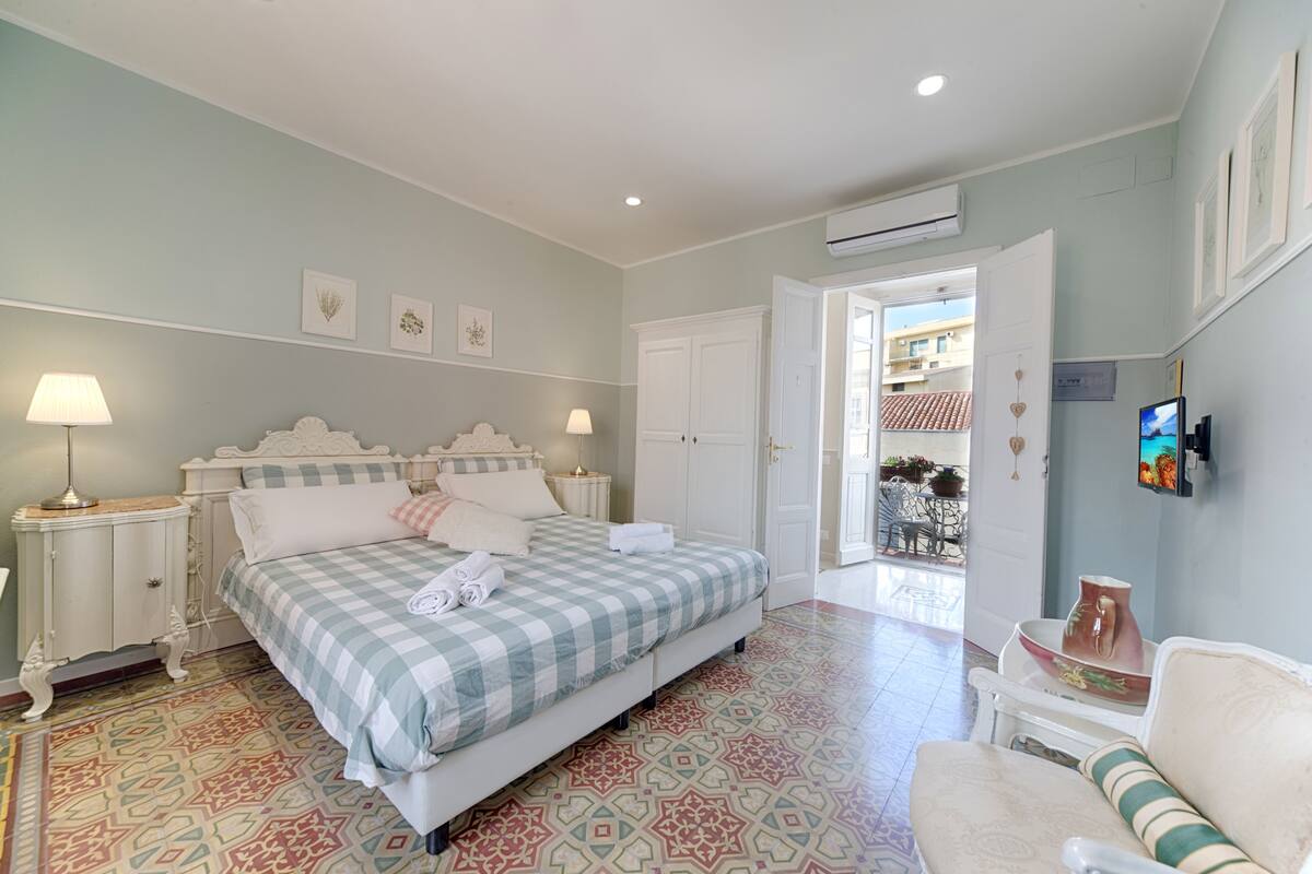 Quarto com colcha xadrez, móveis brancos e ladrilhos estampados.
