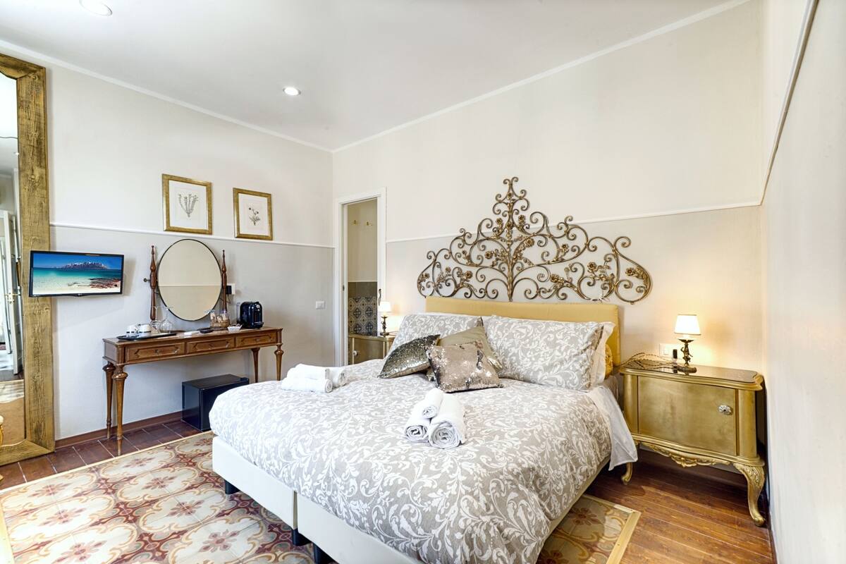 Quarto bem arrumado com cama, mesa de cabeceira, cômoda e televisão em suporte.