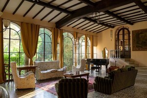 Um quarto amplo com um piano de cauda, vários espaços de estar e grandes janelas em arco.