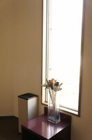 Quarto com janela, um vaso transparente com flores secas sobre uma mesinha e um radiador.