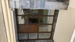 Um canto de um edifício com porta de vidro e janelas, uma ventilação metálica e uma placa na parede.