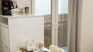 Cozinha compacta com área de refeições, eletrodomésticos brancos e vista por uma porta de correr.
