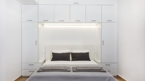 Quarto com cama, duas mesas de cabeceira, guarda-roupa e cabeceira embutida com iluminação.