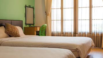 Quarto com duas camas, uma cadeira verde, uma mesa de cabeceira de madeira, um espelho e uma janela com cortinas.
