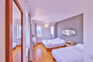 Quarto com duas camas, piso de madeira, um espelho grande e vista para o mar através de uma janela.