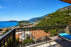 Varanda com vista para uma vila costeira, uma mesa com um copo de vinho tinto e uma almofada azul.