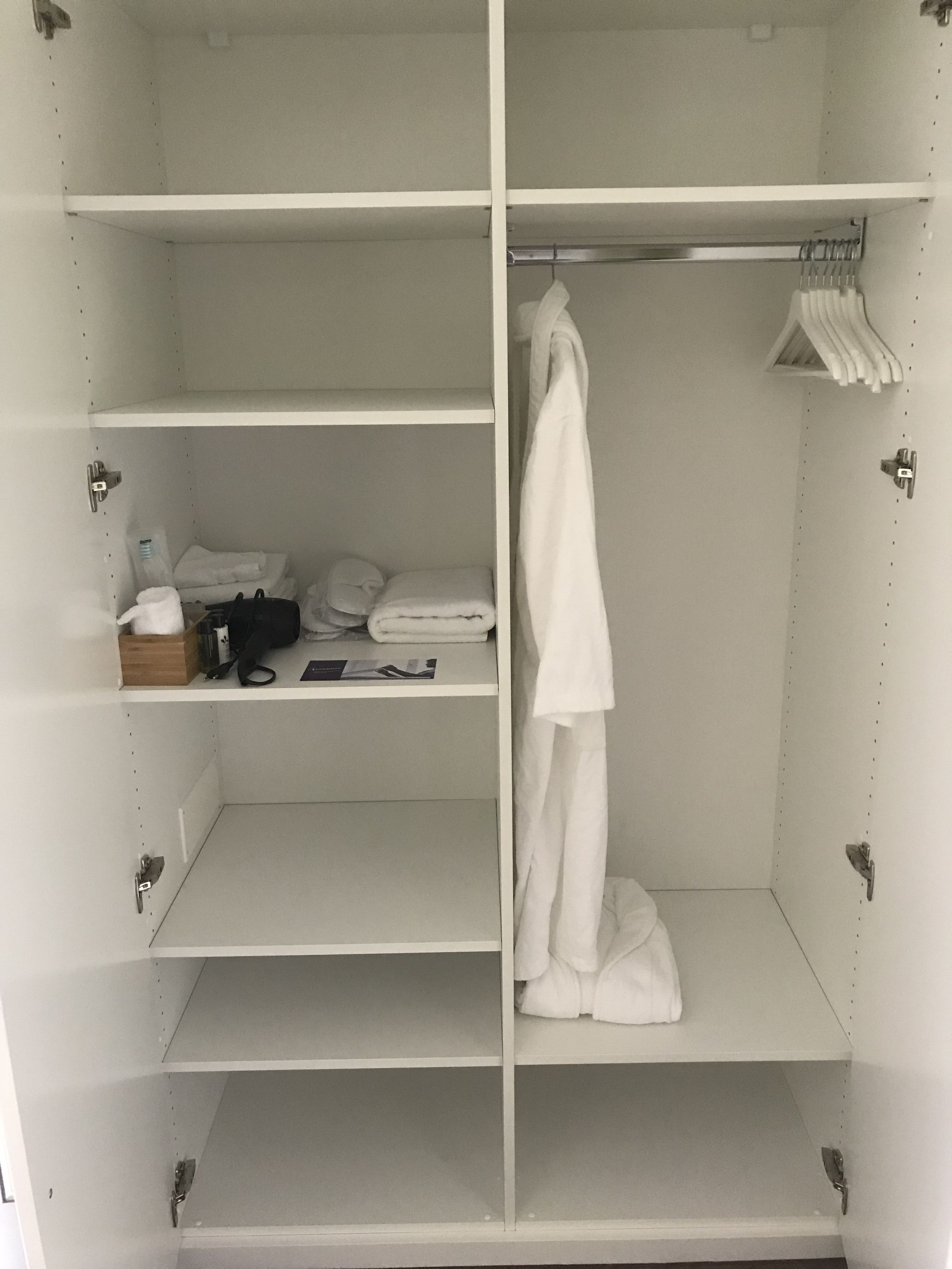 Um closet amplo e aberto, com diversas prateleiras e espaço para pendurar roupas, contendo toalhas dobradas e alguns objetos pessoais.