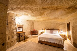Quarto de paredes de pedra com uma cama de madeira, uma mesa de cabeceira e um espelho.