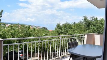 Varanda com mesa e cadeiras, oferecendo uma vista panorâmica da costa, com vegetação e edifícios.
