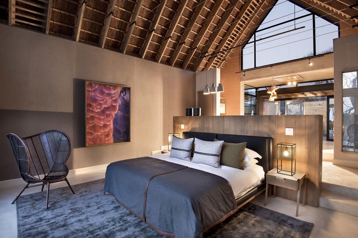 Quarto moderno com cama grande, uma cadeira, um quadro e um claraboia.