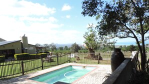 Piscina com deck de madeira e mesa de piquenique, cercada por uma vedação e árvores.