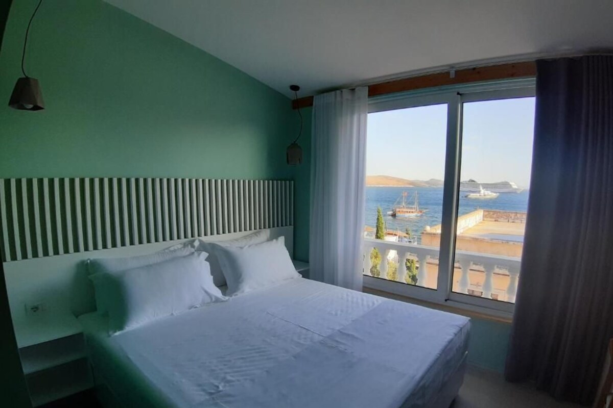 Quarto de hotel com uma cama grande, vista para o mar e uma janela com cortinas.