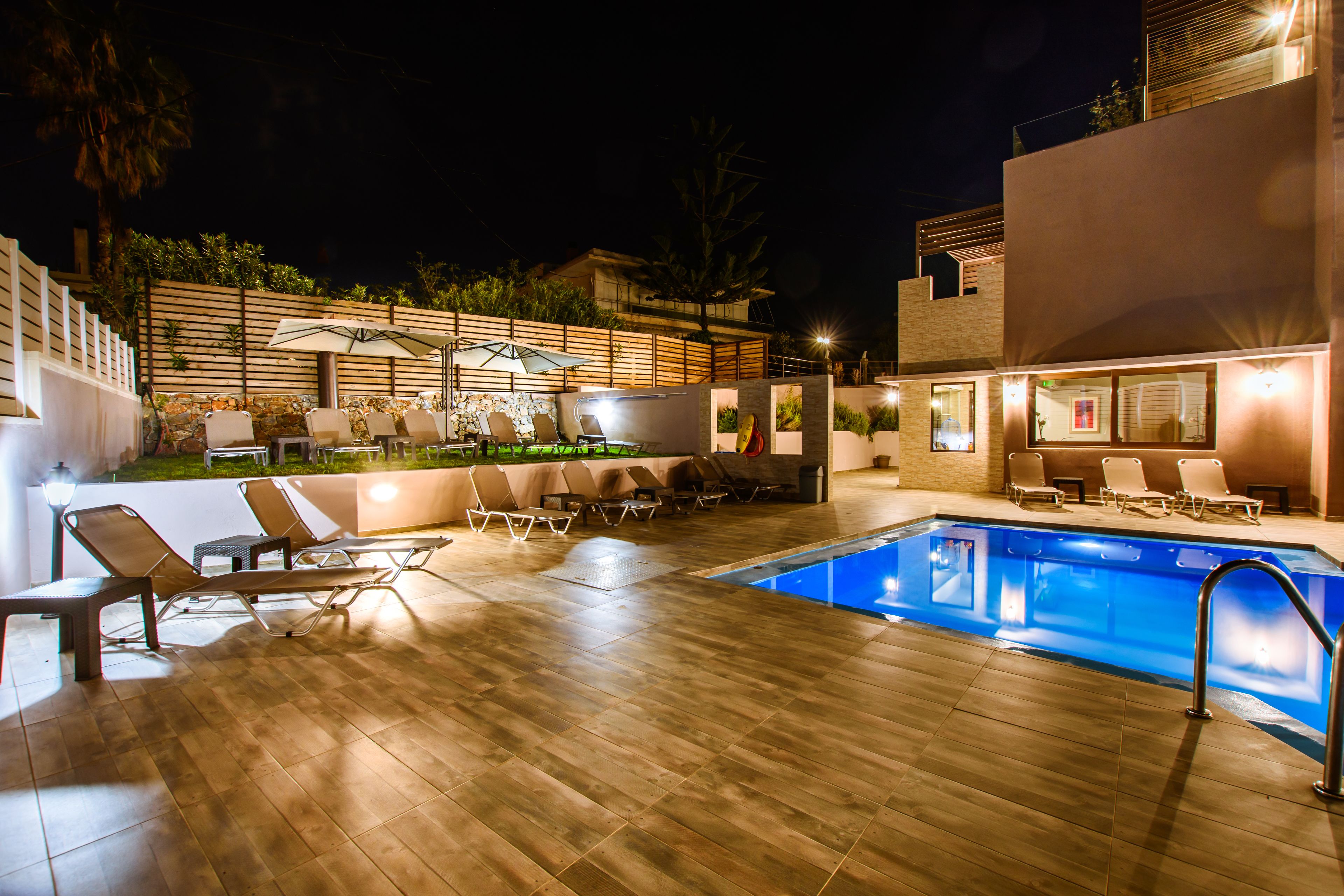 Uma área de piscina ao ar livre à noite, com espreguiçadeiras, uma piscina e um pátio bem iluminado.