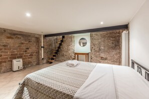 Quarto com uma cama grande, escada de madeira, espelho redondo e radiador.