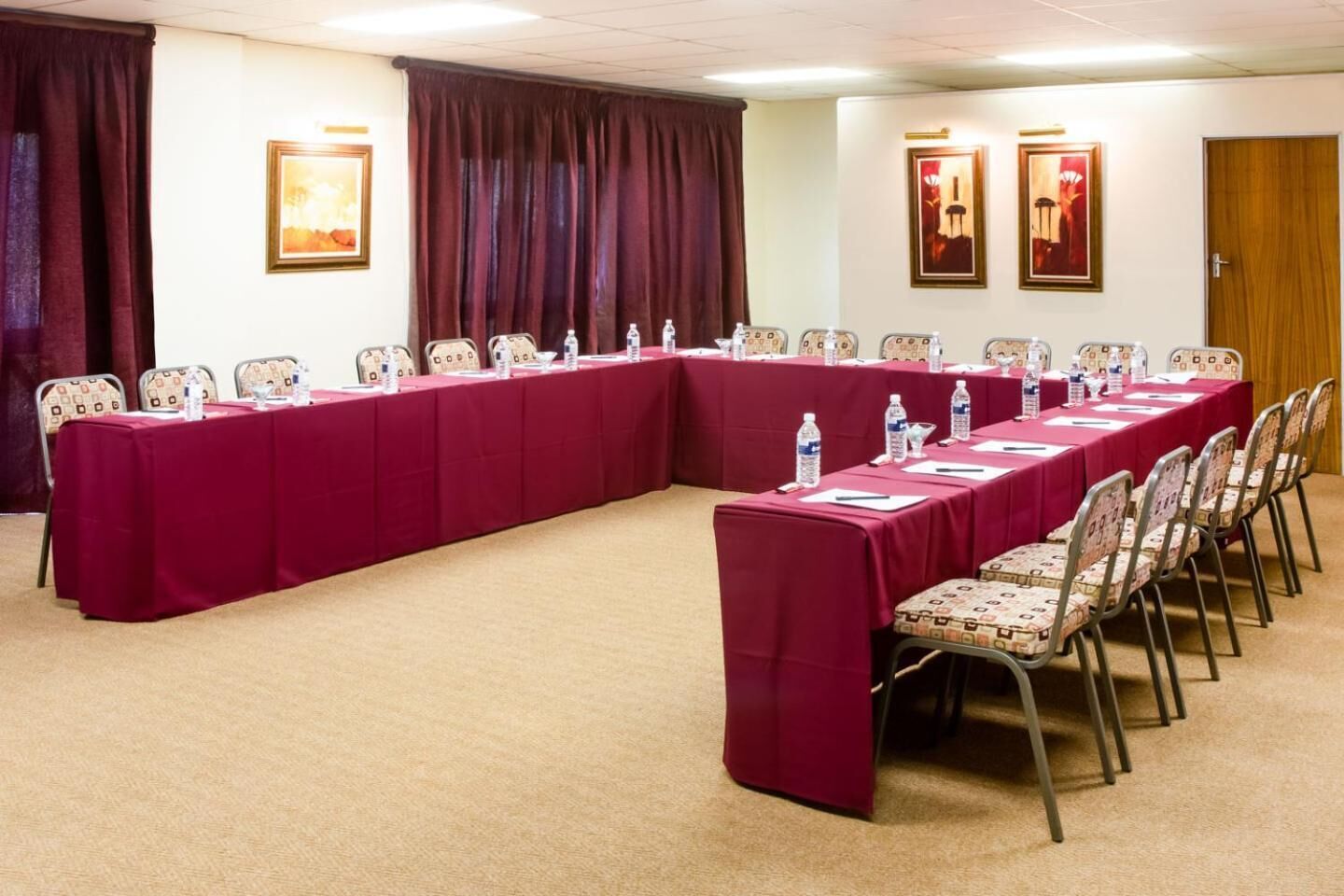 Uma sala de conferências com uma mesa comprida, cadeiras e garrafas de água.