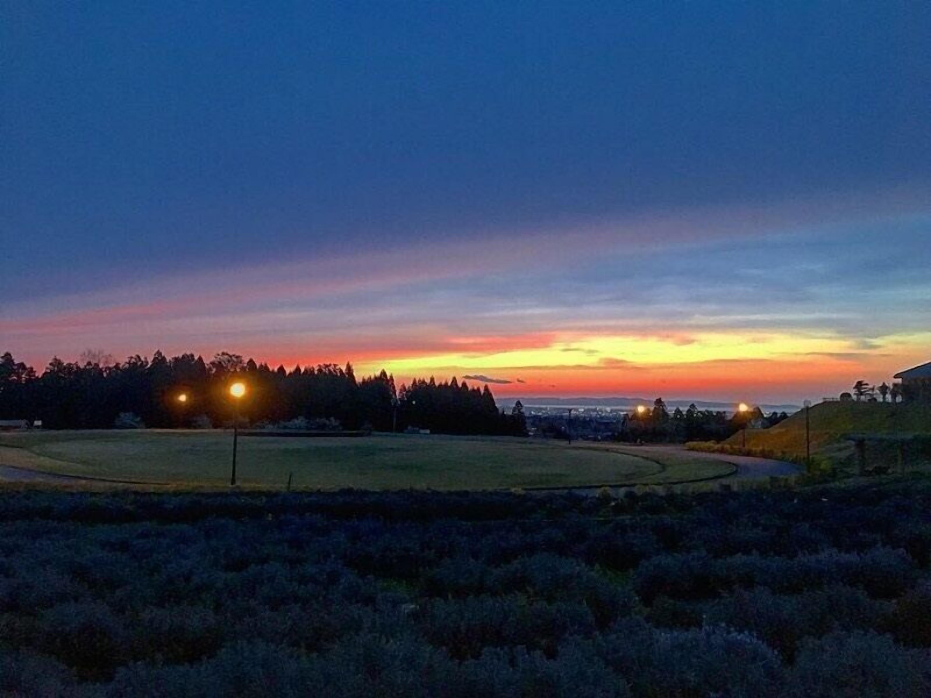 Vista do pôr do sol sobre um campo de golfe, com céu limpo e luzes da cidade ao longe.
