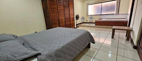 Quarto com cama, guarda-roupa de madeira, um banco e janela com vista.